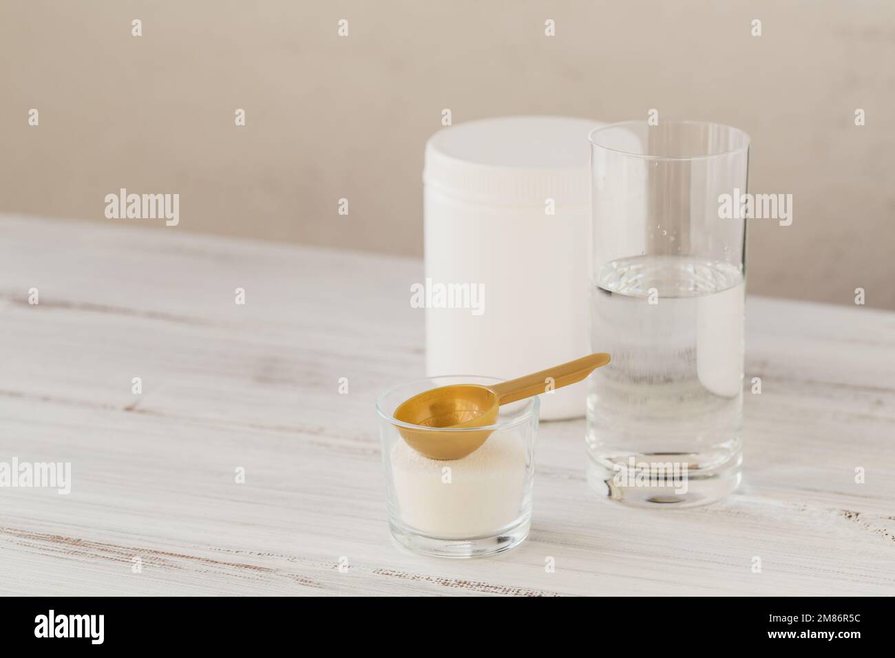 Collagen powder in bowl, glass of water and measure spoon on a white ...