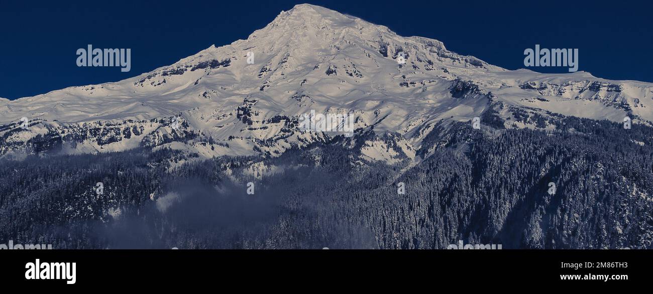 A majestic and rugged snowy mountain stands tall against a clear blue ...