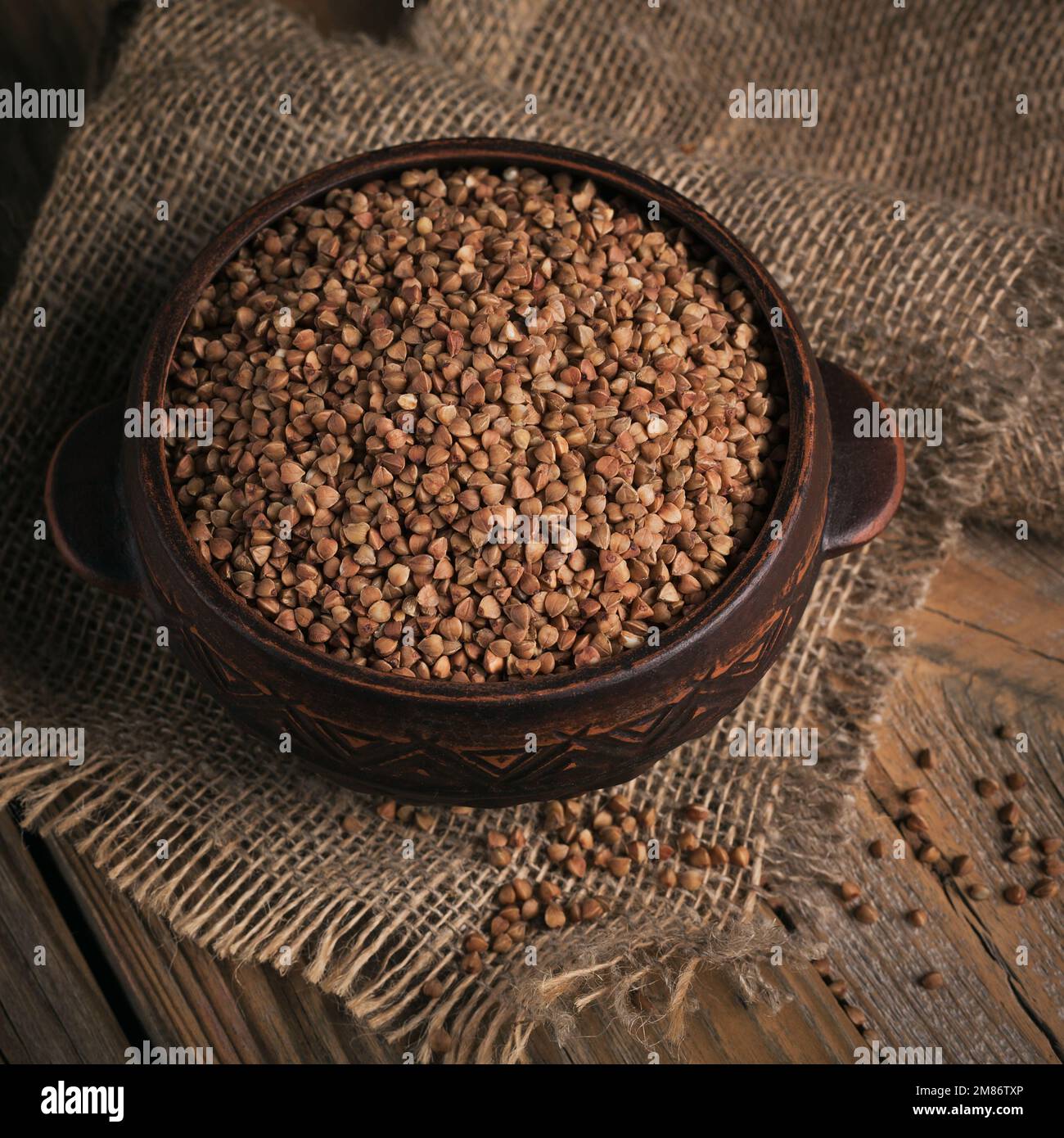 Organic uncooked scattered buckwheat grain in a bowl on a rustic wooden ...