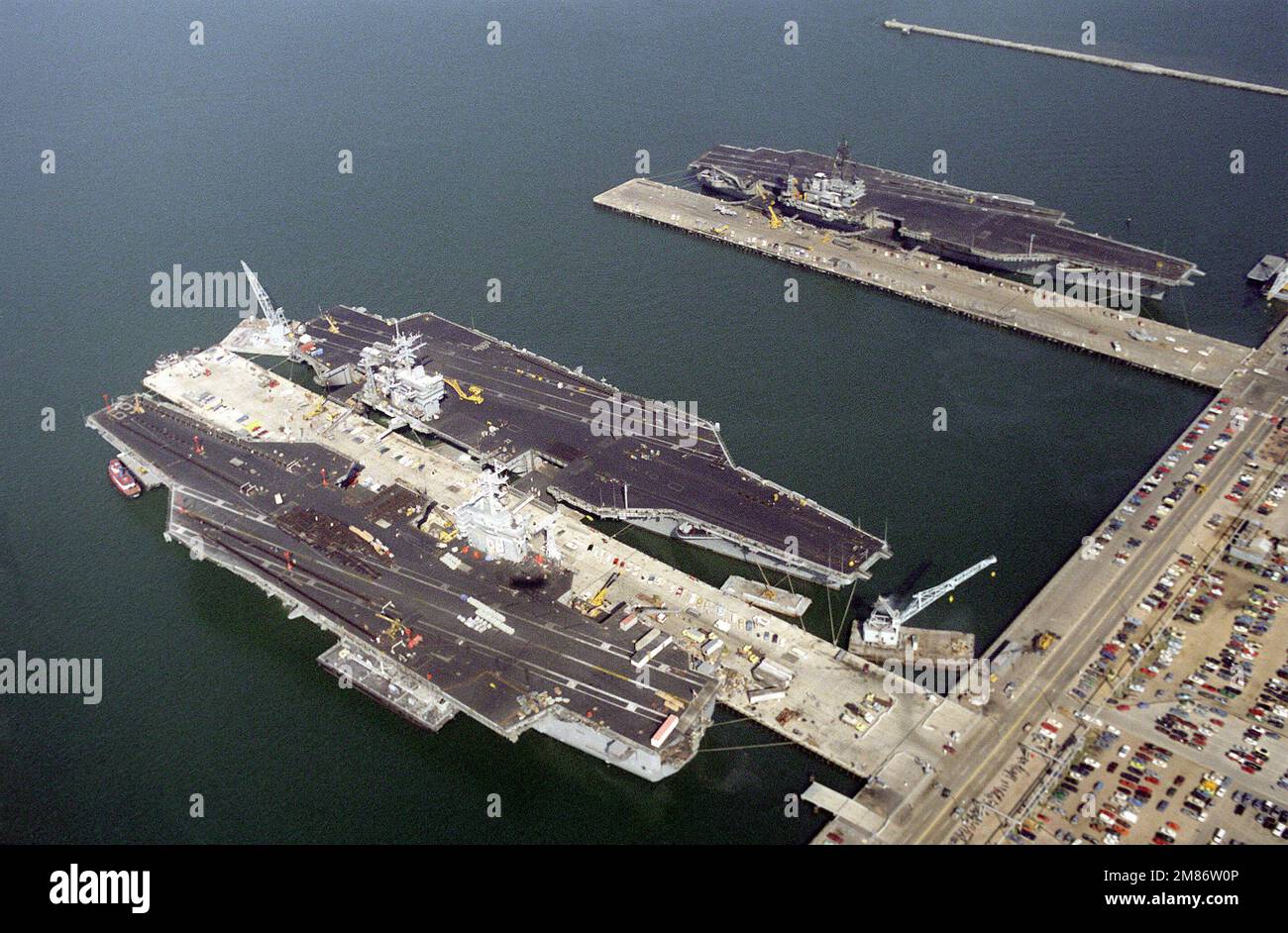 An elevated view of three aircraft carriers docked at piers. They are ...