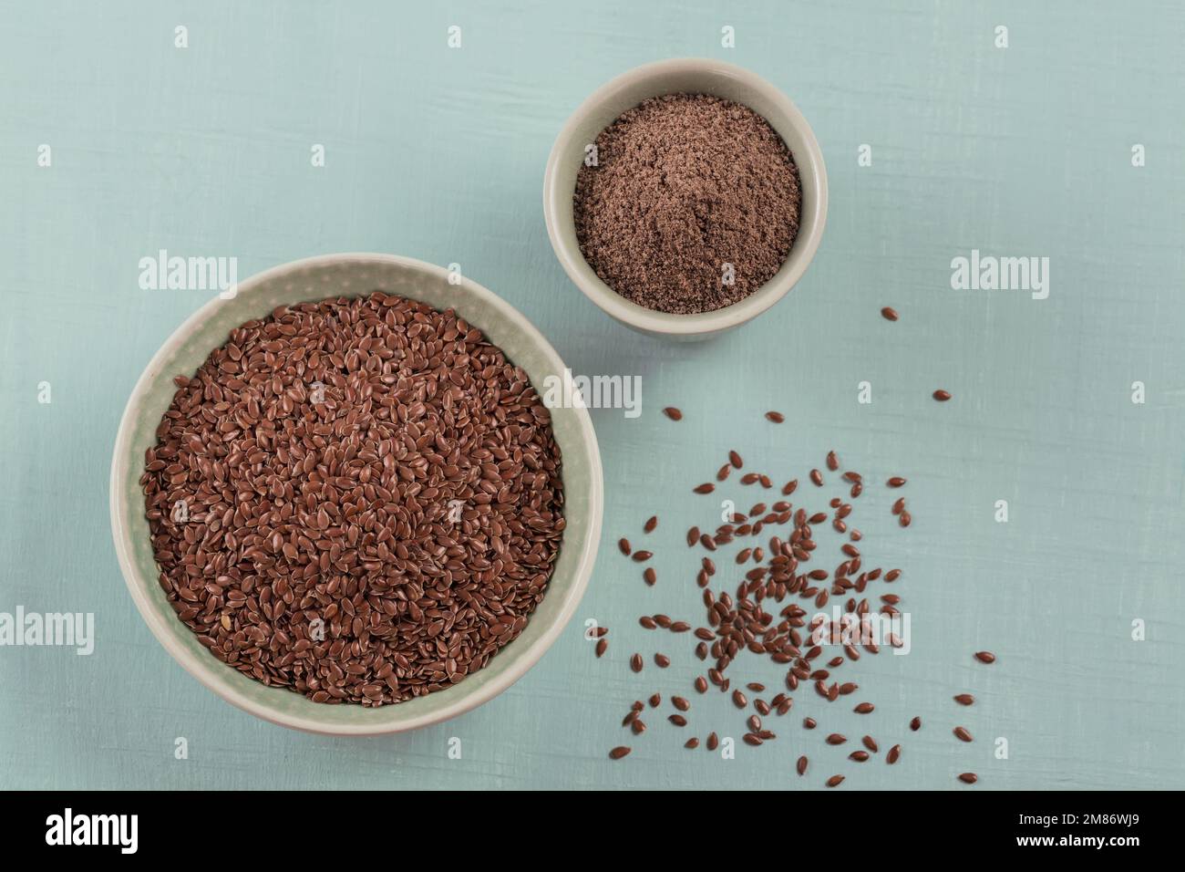 Brown flax seed and ground or crushed flaxseed or linseed in small bowl on a light blue ...
