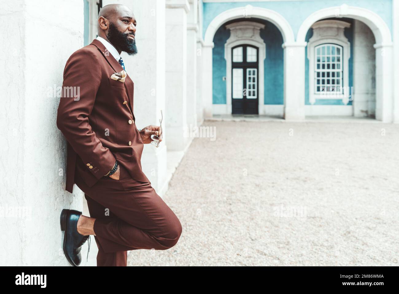A black man with an unshaven beard wearing a Bordeaux suit leaned ...