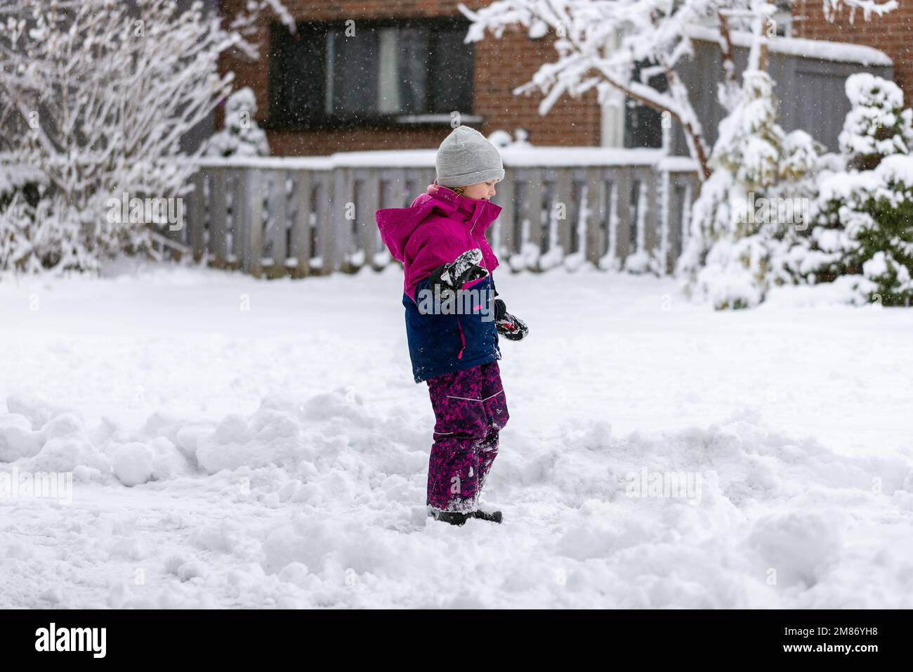 Happy child playing with snow outdoors near house in winter. Wintertime ...
