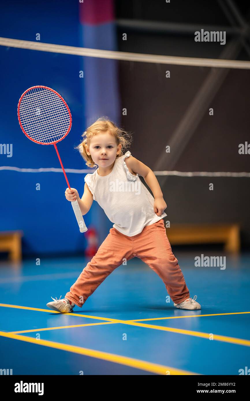 Little girl three years old playing badminton in sport wear on indoor ...