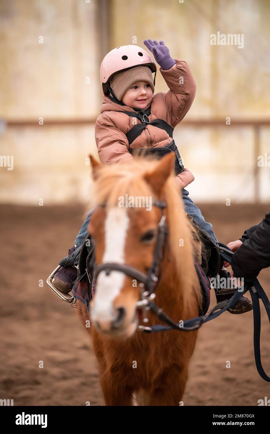 Little Child Riding Lesson. Three-year-old girl rides a pony and does ...