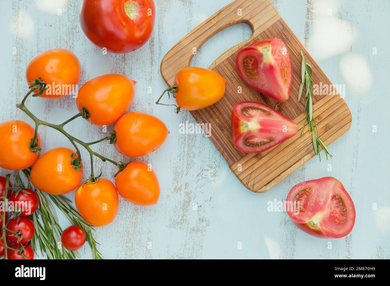 Various colorful tomatoes and rosemary herb on a light blue background ...