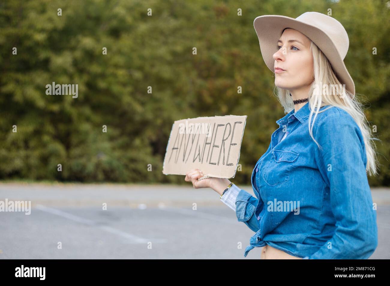 Tired woman hopefully look out passing cars with cardboard poster on ...