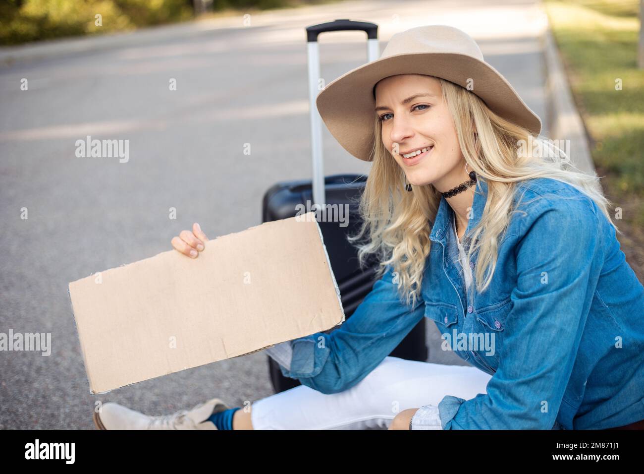 Happy woman hopefully wait passing car sitting with suitcase and ...
