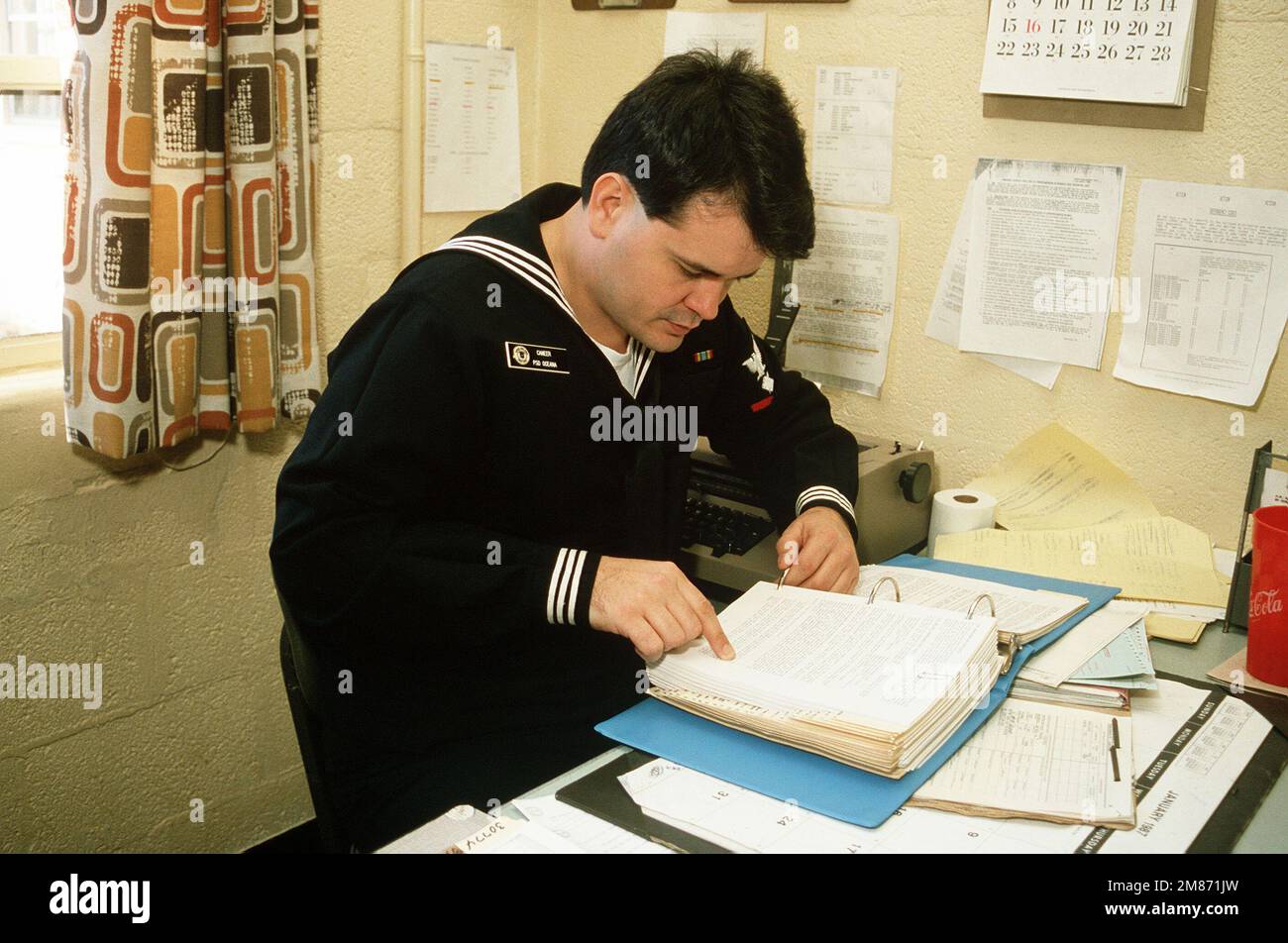 A personnelman consults a manual while reviewing a service record book ...