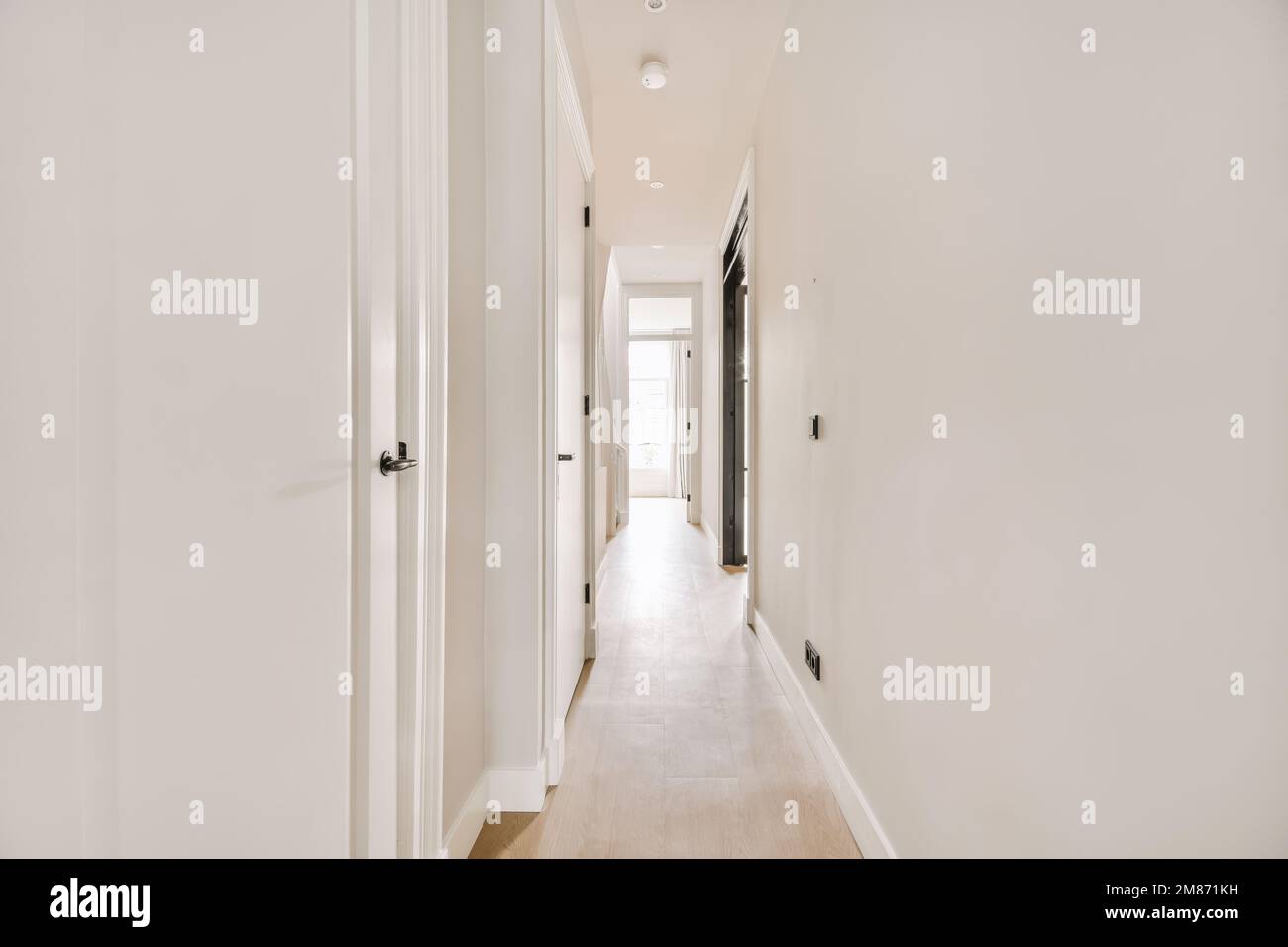 a long hallway with white walls and wood flooring on either side by ...