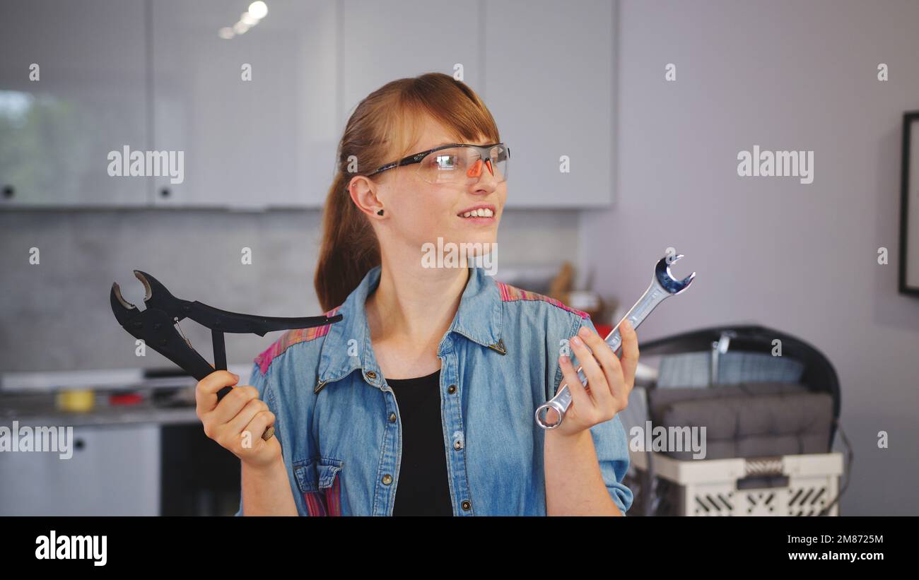 young Caucasian woman with safety glasses holding a spanner and pincers ...
