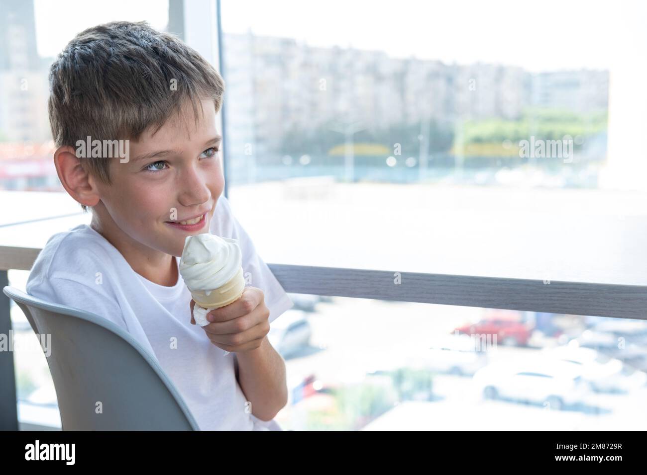 A cute teenage boy eats a swirling white ice cream in a waffle cup ...