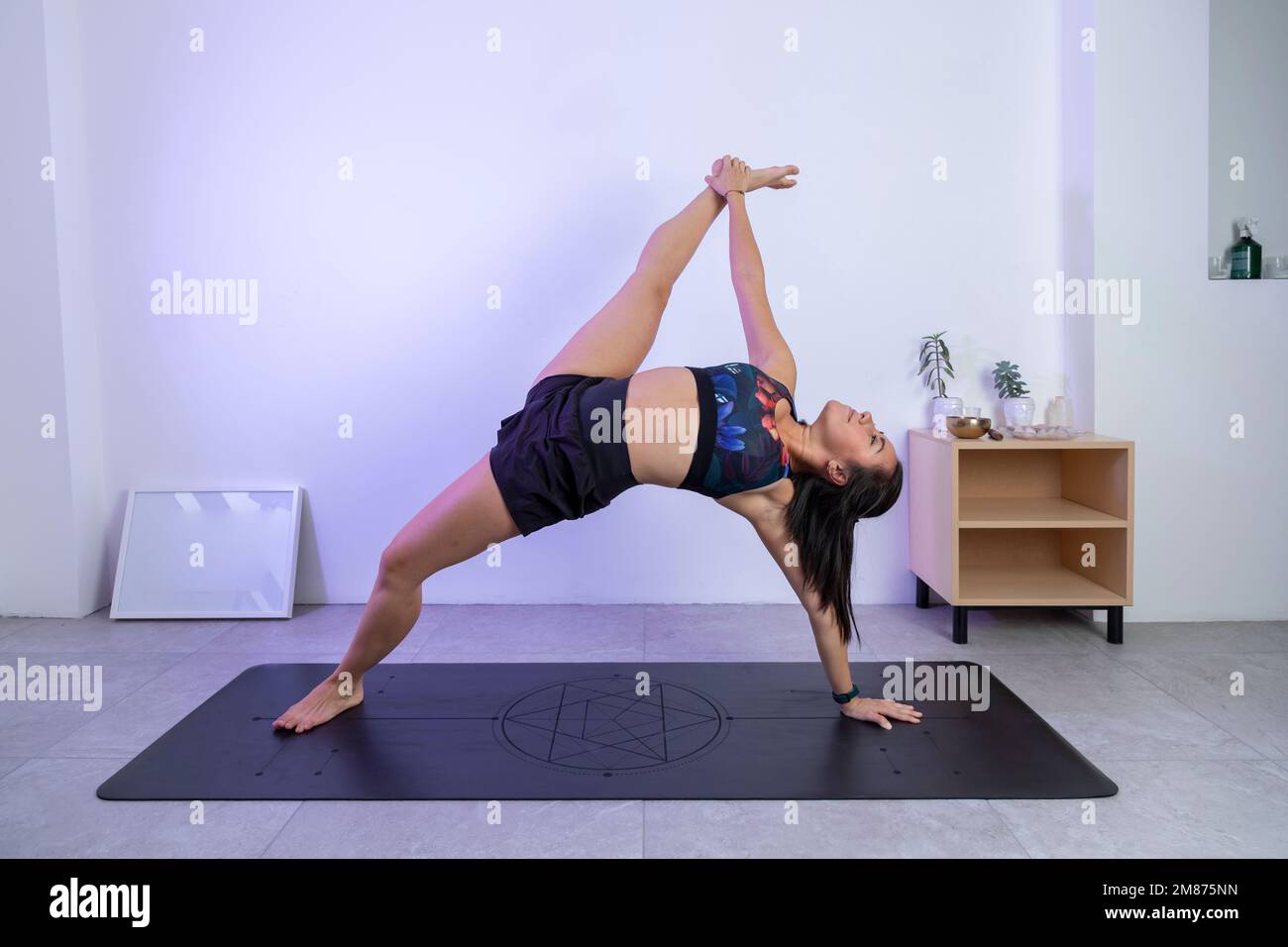 Young woman holding foot and raising hip while doing yoga pose in ...