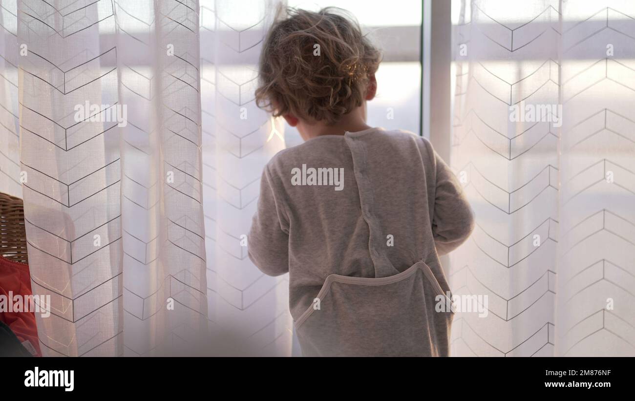 Toddler boy standing by window looking outside in the morning2 Stock ...