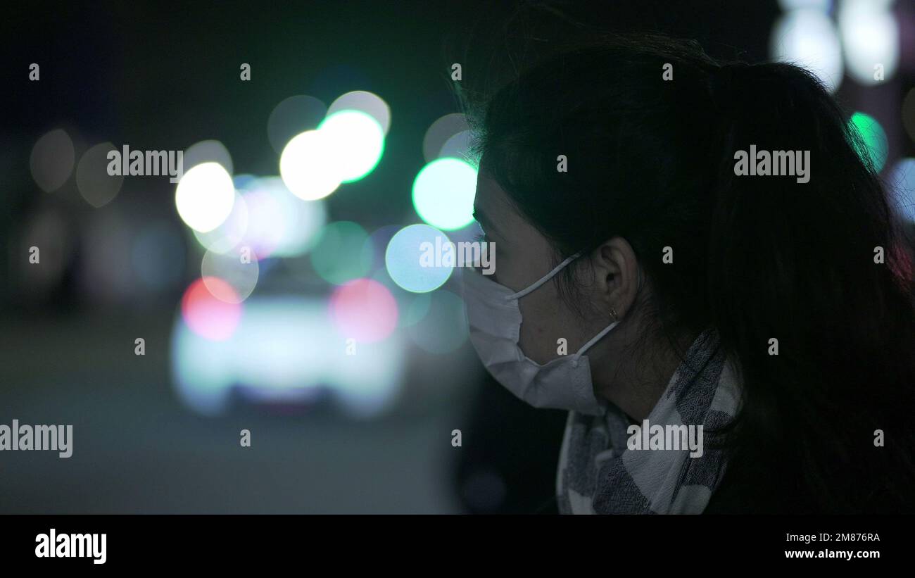 Woman wearing covid-19 face mask at night waiting to cross street in ...