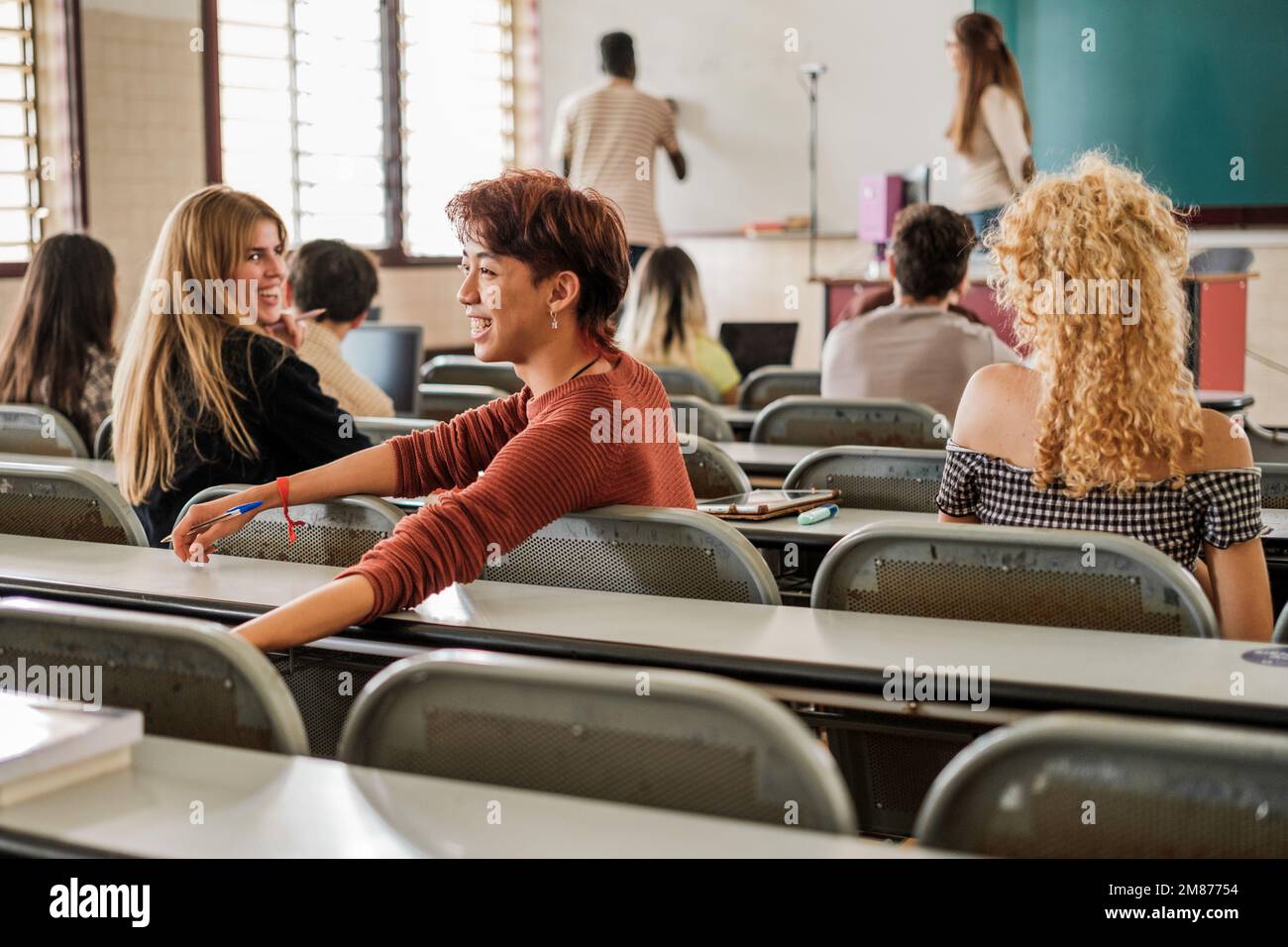 Young people in university class talking while a classmate explains on ...