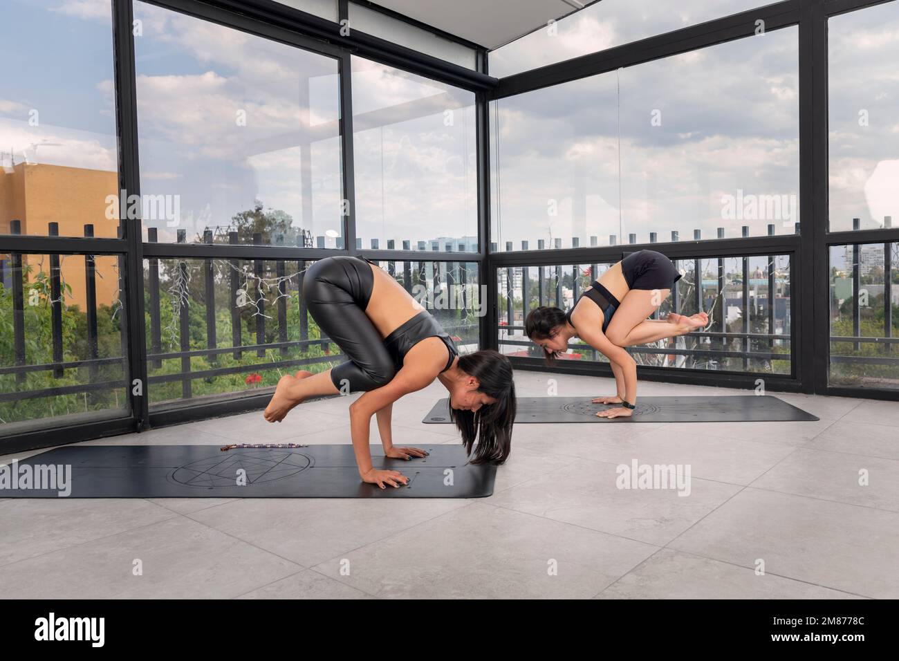 Two young women in front of yoga studio windows, doing half lotus crow ...