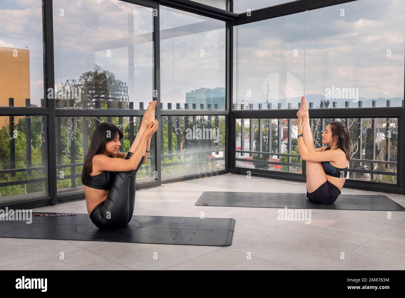 Two beautiful young Latin women doing advanced yoga poses in the studio ...