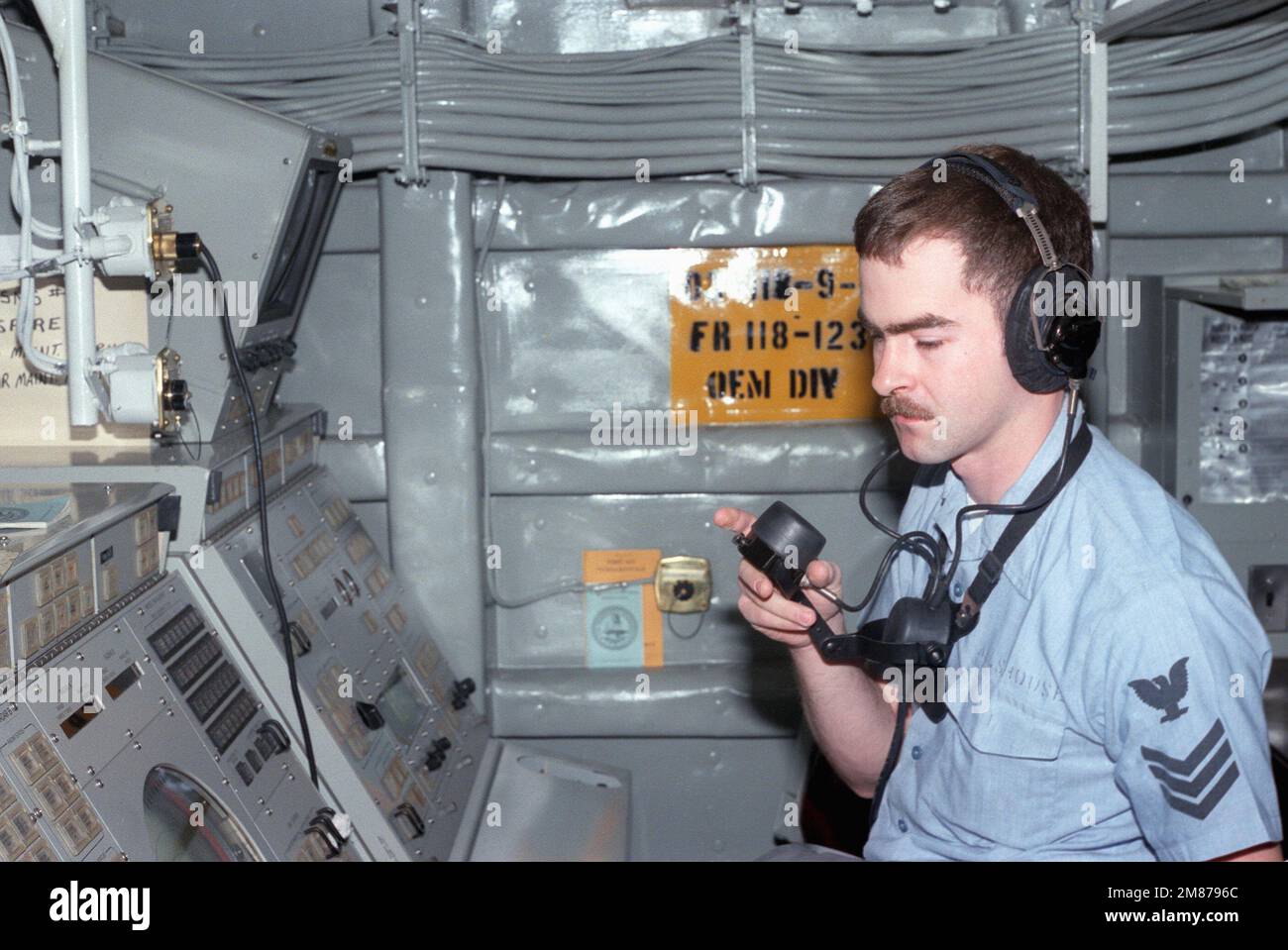 A phone talker stands by a console in the fire control room aboard the ...