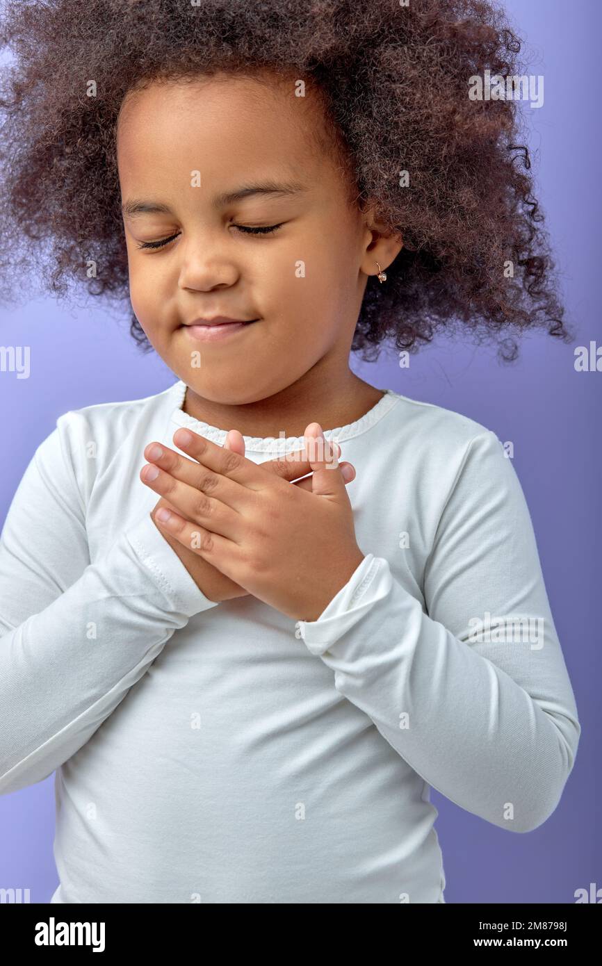 Faithful little girl closes eyes and keeps hands on chest near heart ...