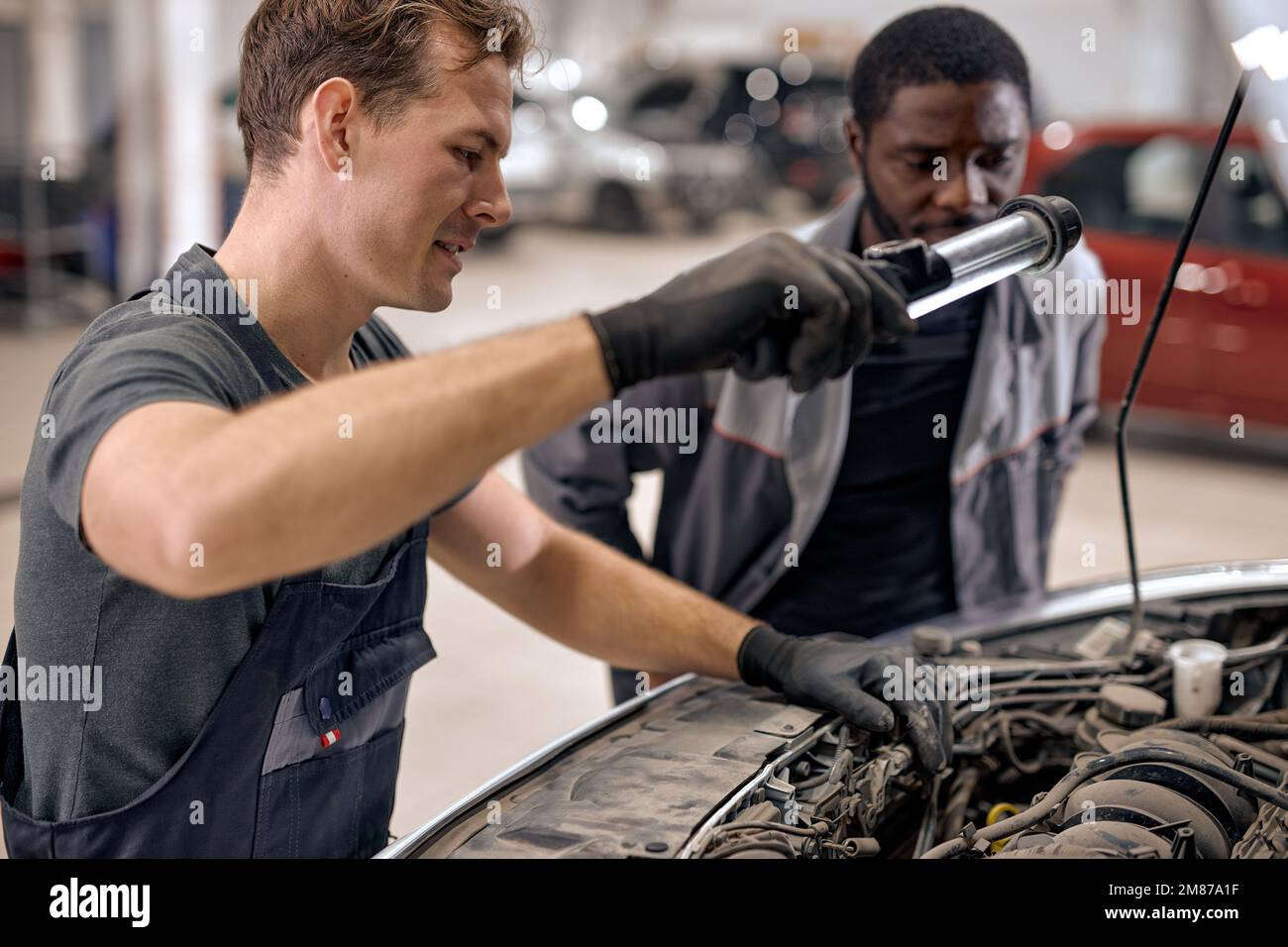 two young diverse mechanics checking car hood in auto service ...