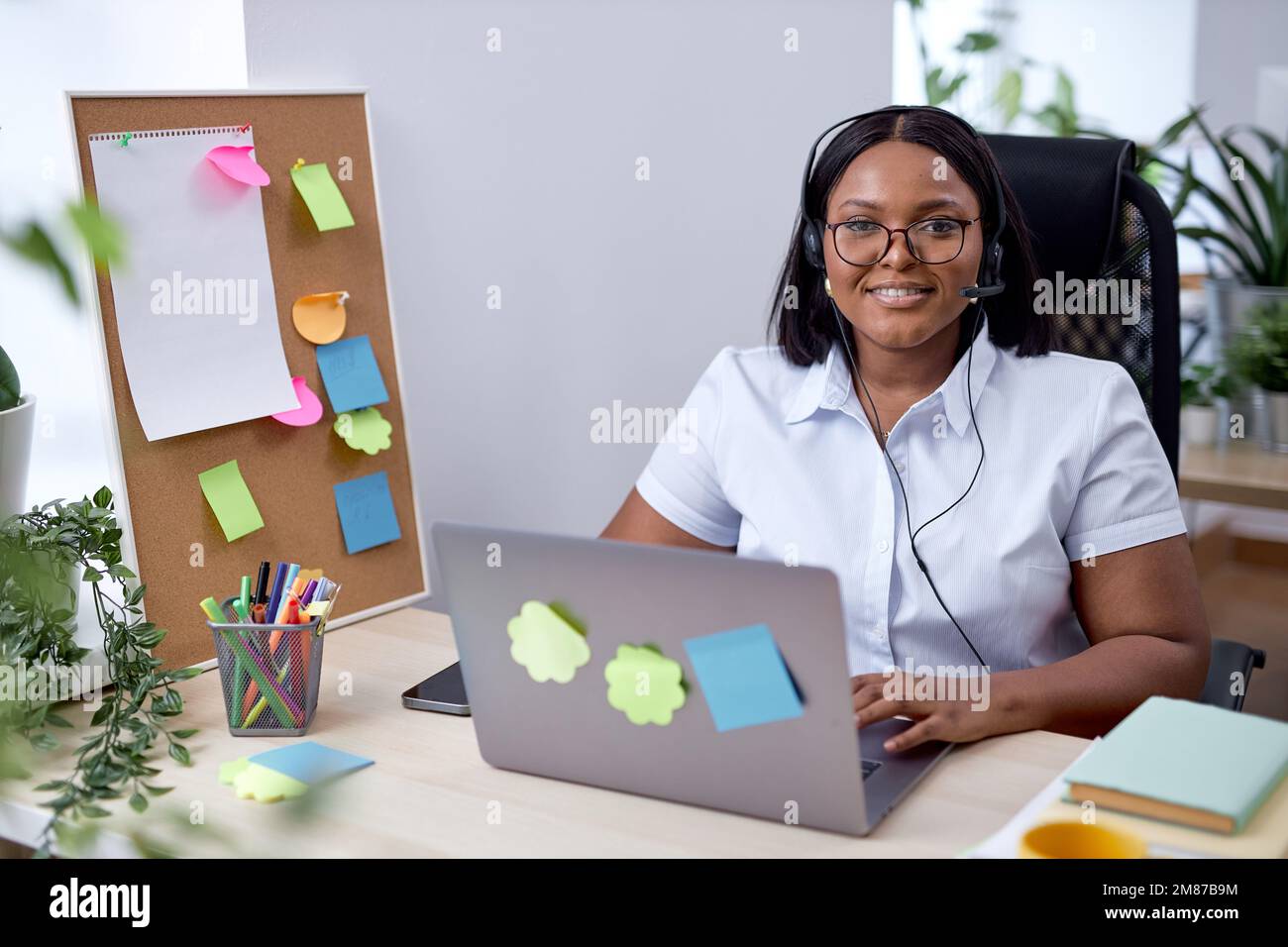 Adorable smiling black female dispatcher with microphone working alone ...