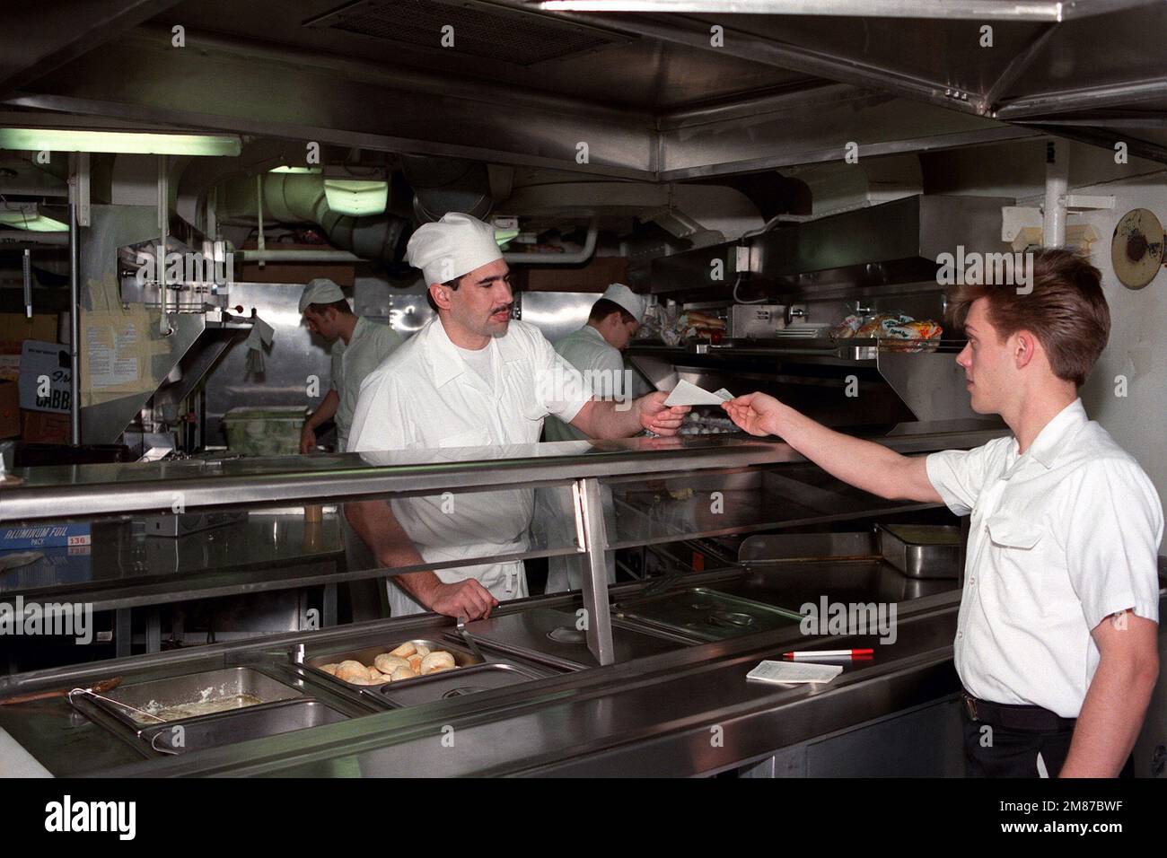 A messman delivers a meal order from the wardroom to a cook in the ...