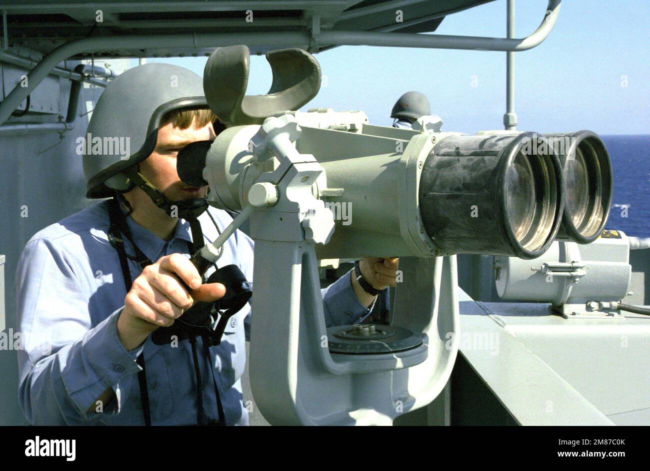 A crewman wearing a sound-powered phone looks through the ship's ...