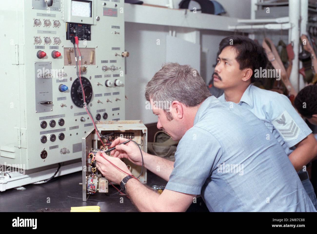 A sailor works on a piece of electrical equipment with the help of a ...