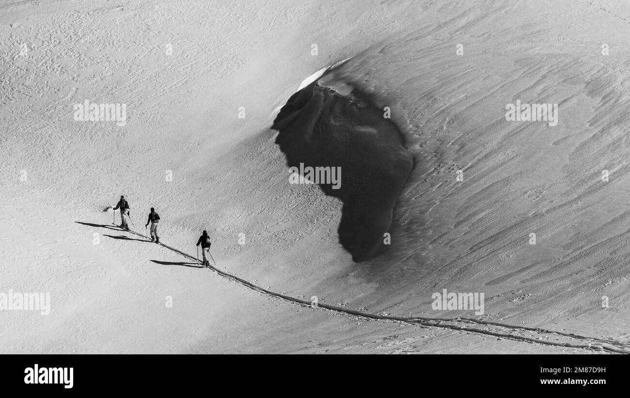A grayscale beautiful view of skiers on a snowy mountain during sunrise ...