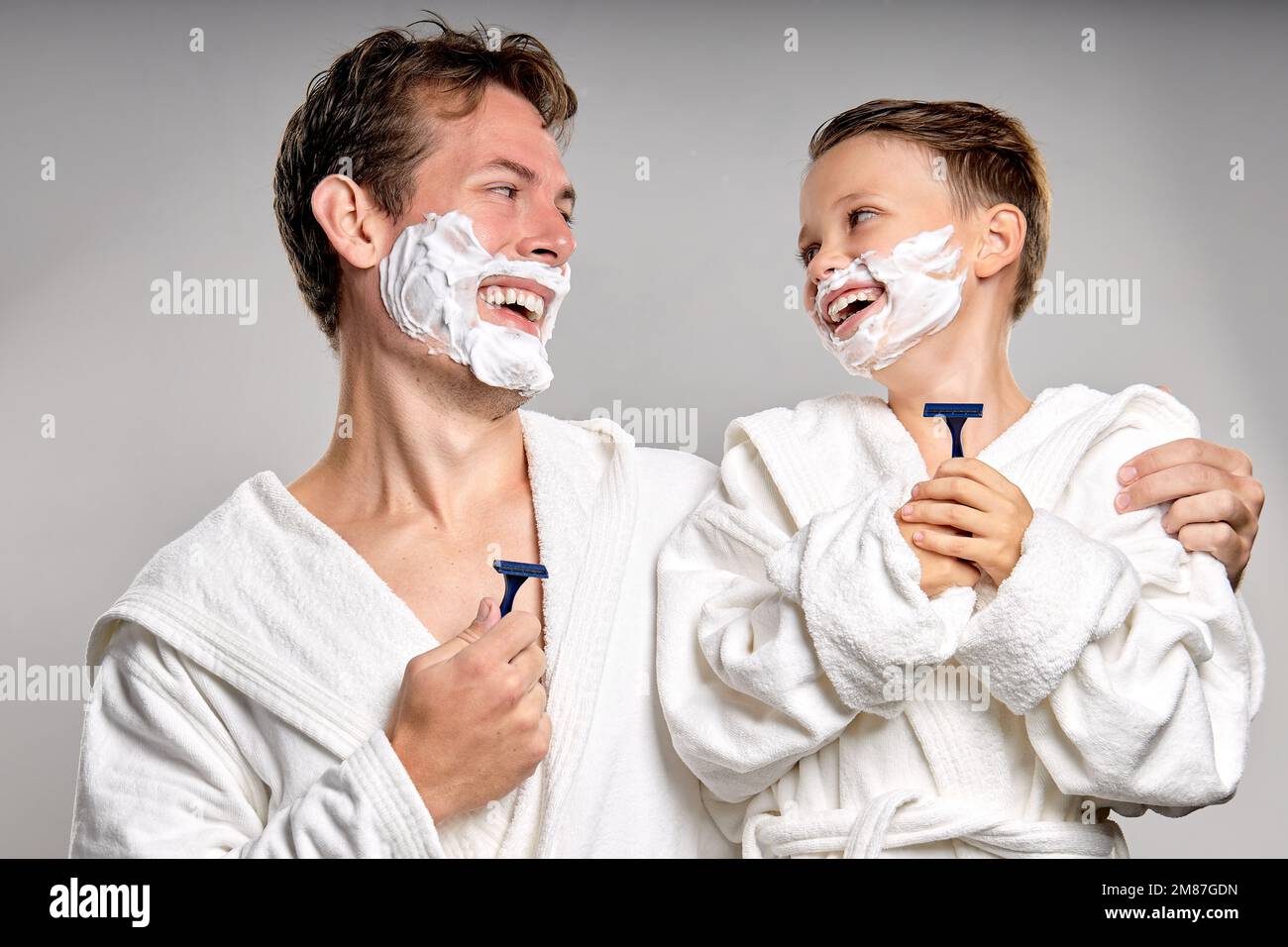 Happy dad and son with pleasant appearance, have shaving foam on faces ...