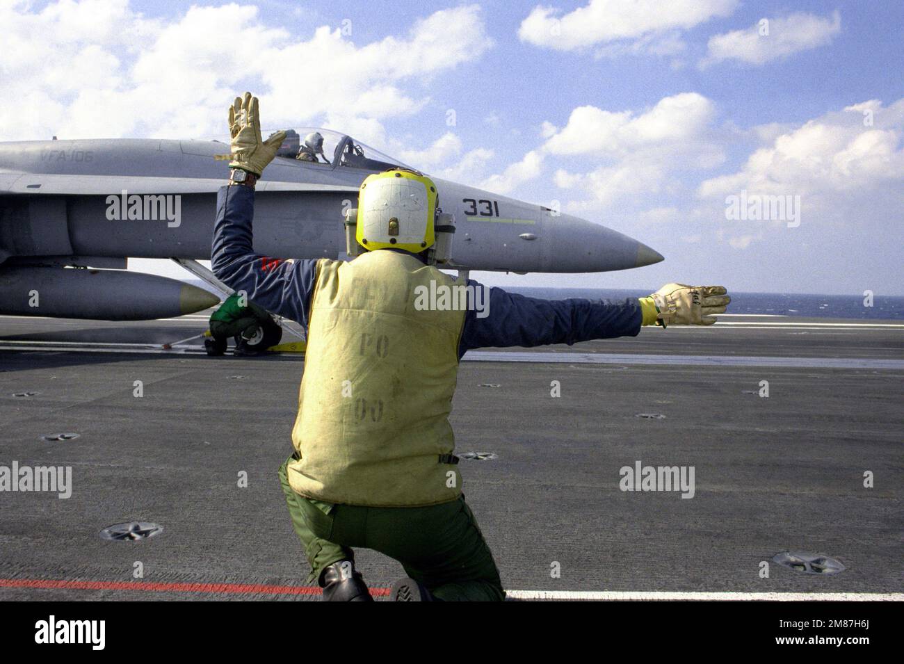 A flight deck crew member signals to the pilot of an F/A-18 Hornet ...