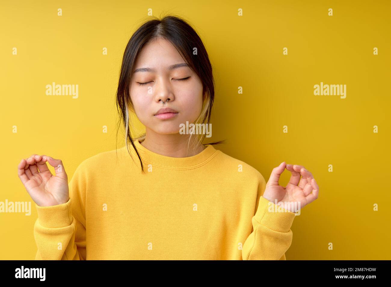 Portrait of attractive, adult asian female Wearing yellow shirt meditating, keeping eyes closed ...