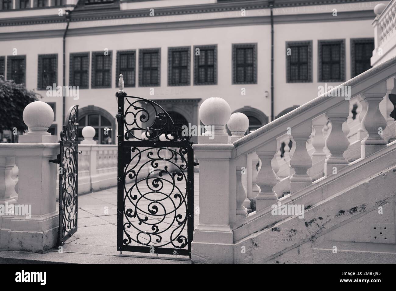 A grayscale of an opened metal forging gate and white stone stair case ...
