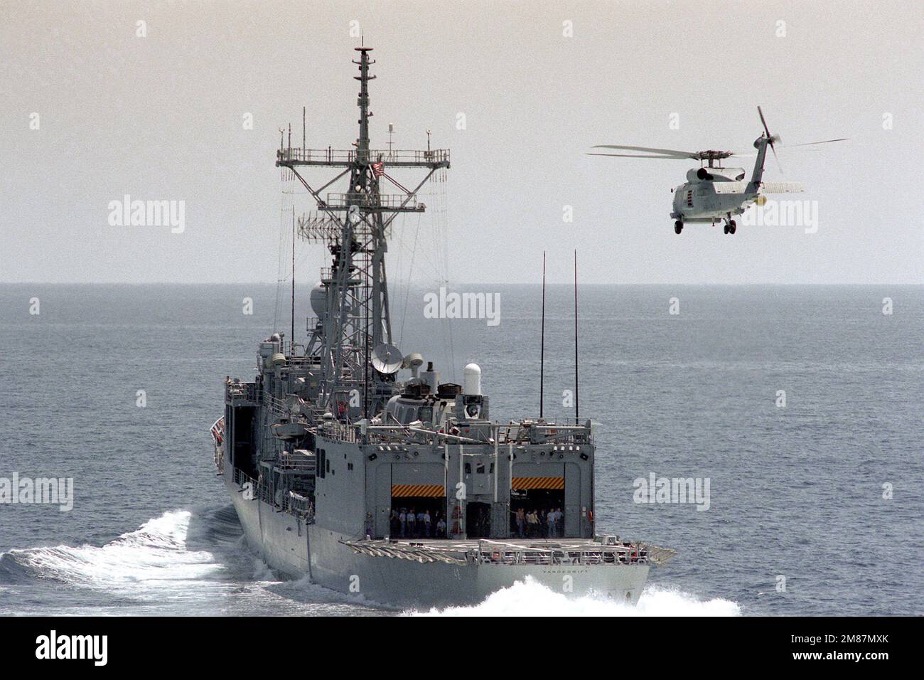 Crew members watch from the hangar bays as aSH-60B Seahawk helicopter ...