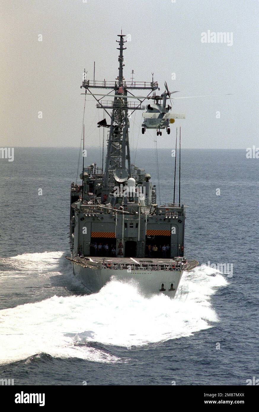 Crew members watch from the hangar bays as an SH-60B Seahawk helicopter ...