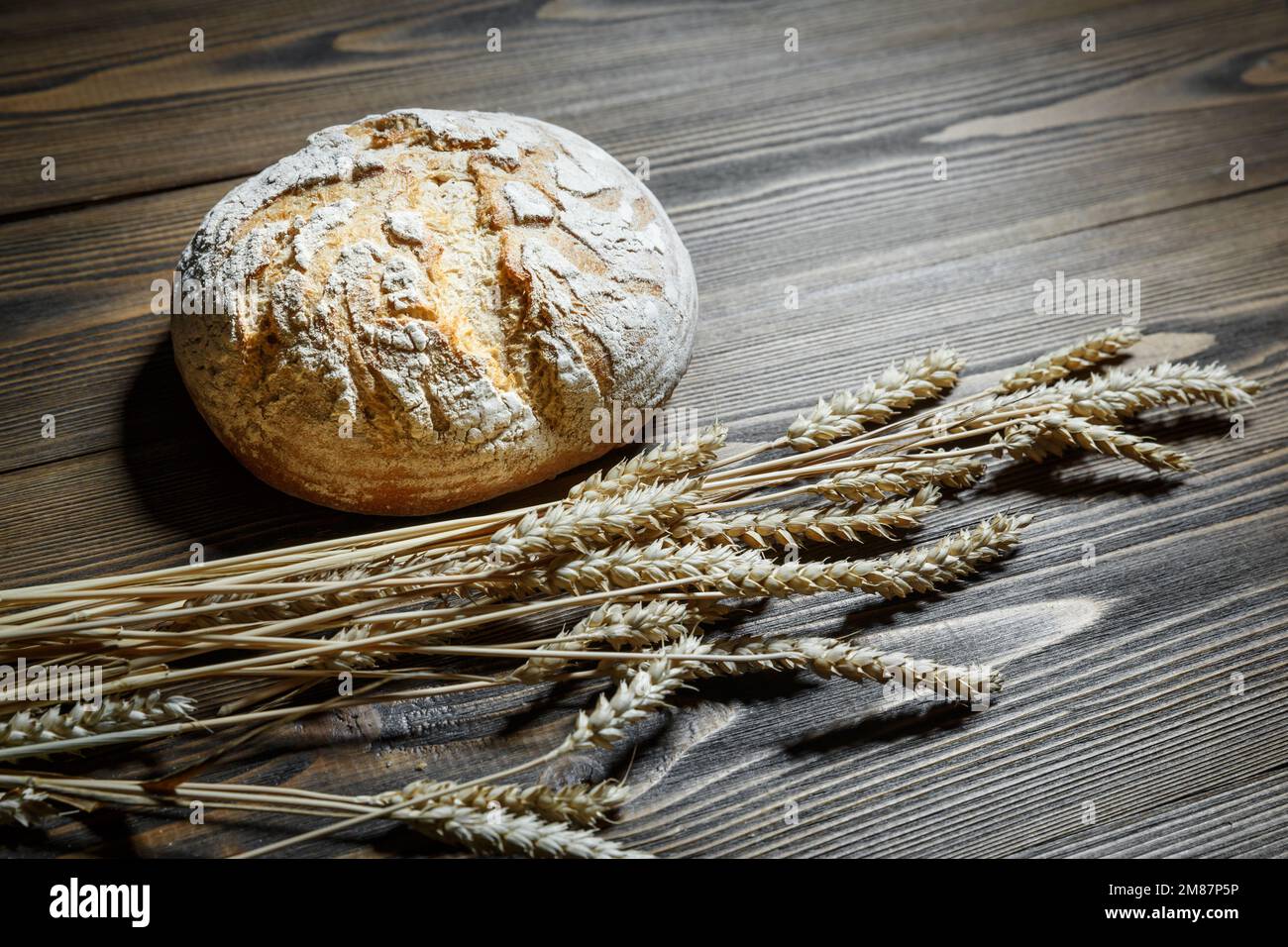 Fresh baked bread loaf and wheat ears lying on a wooden background ...