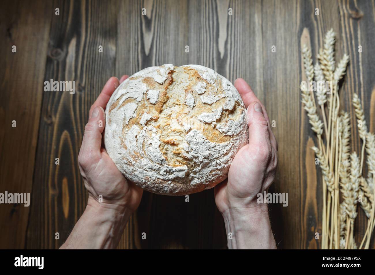 Male hands holding fresh baked bread loaf over wood background. Food ...
