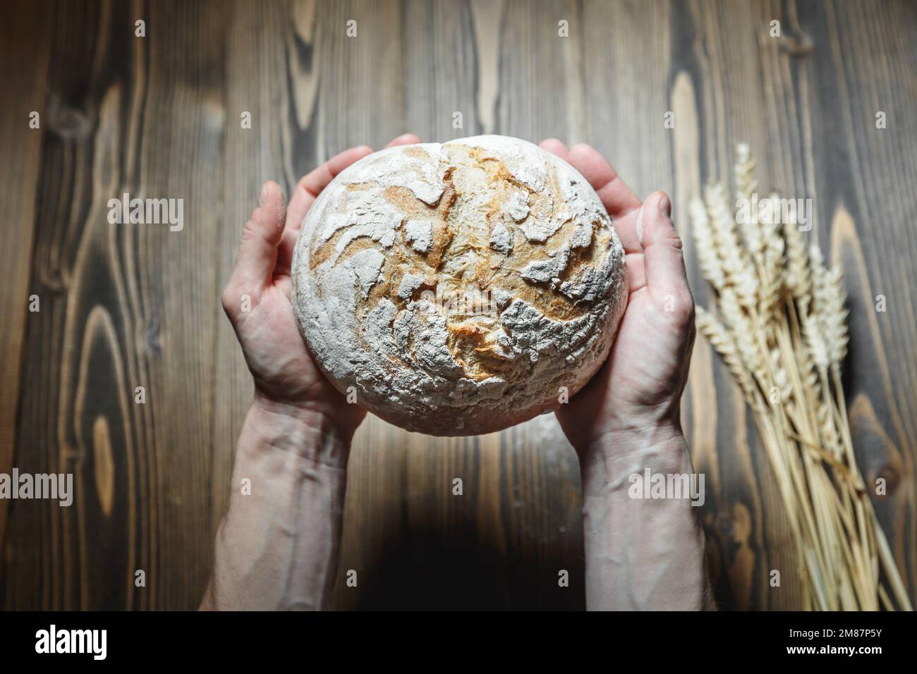 Male hands holding fresh baked bread loaf over wood background. Food ...
