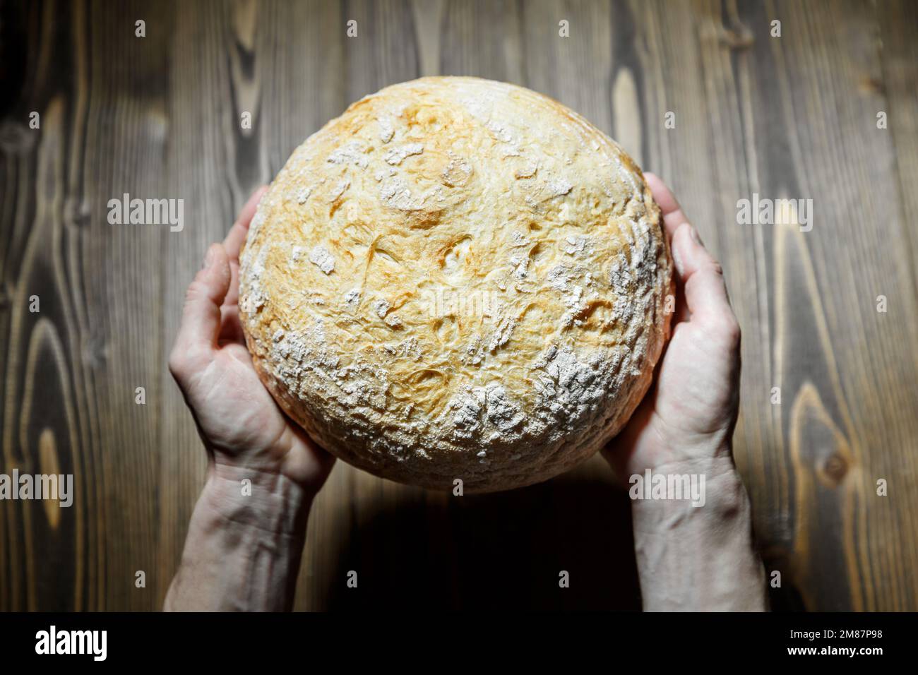 Male hands holding fresh baked bread loaf over wood background. Food ...