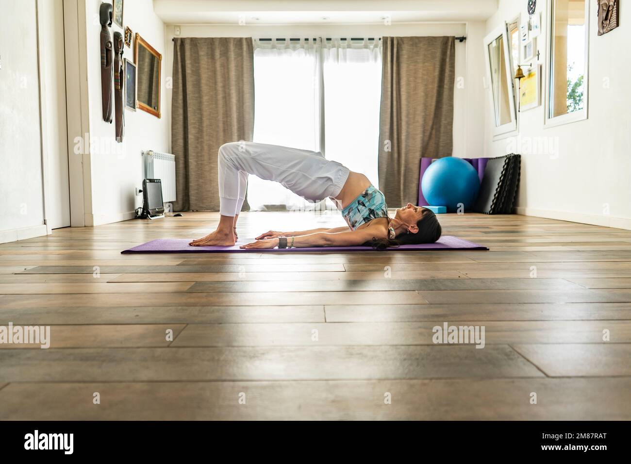 Side view of a woman practicing yoga, doing Bridge Pose (Setu Bandha ...