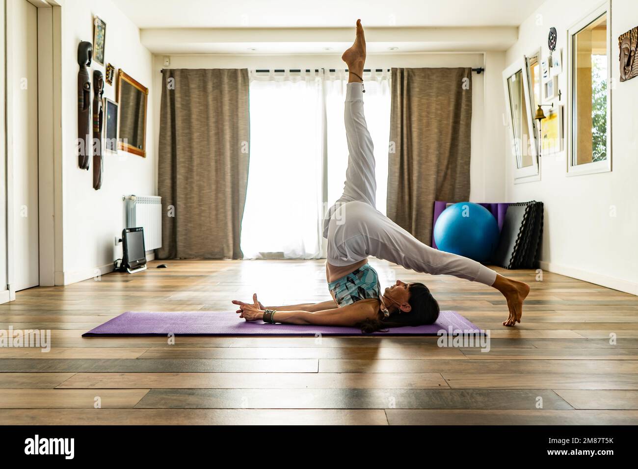 Side view of a woman practicing yoga, doing One Legged Shoulder Stand ...