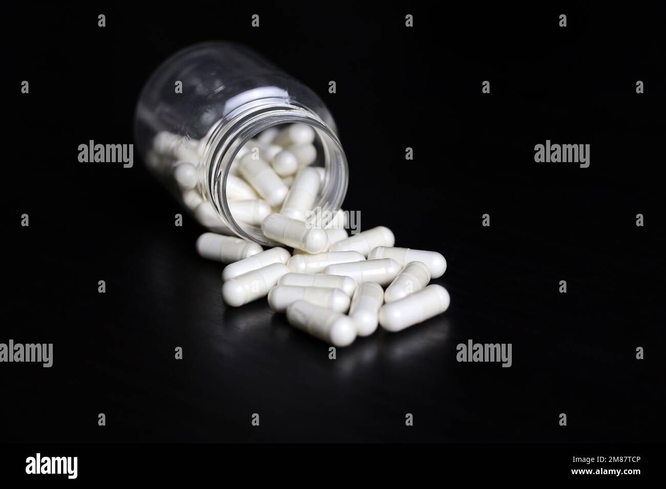 White pills on a black wooden table, medication in capsules scattered ...