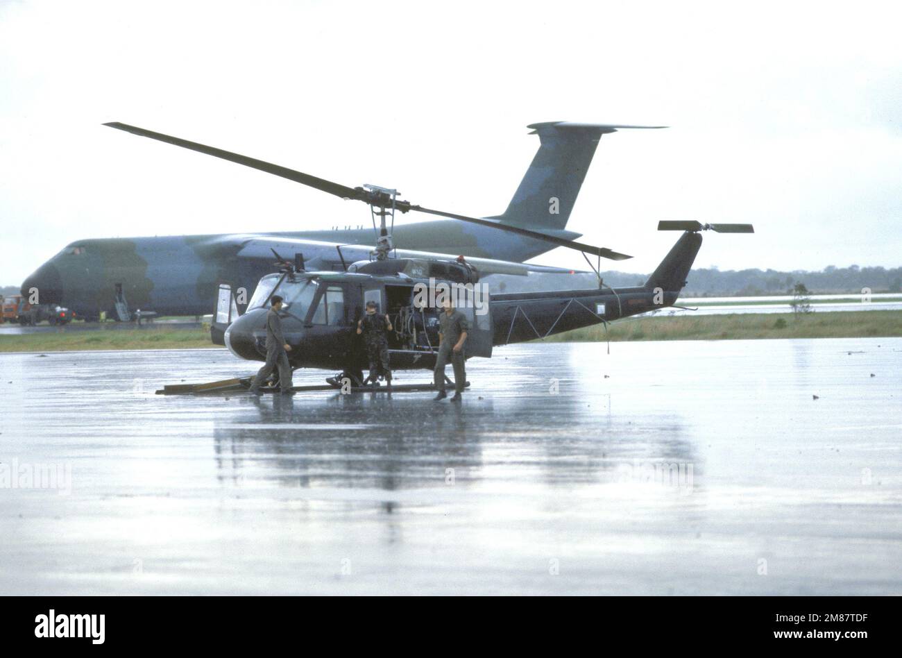 Servicemen stand in the rain prepare to board a UH-1 Iroquois ...