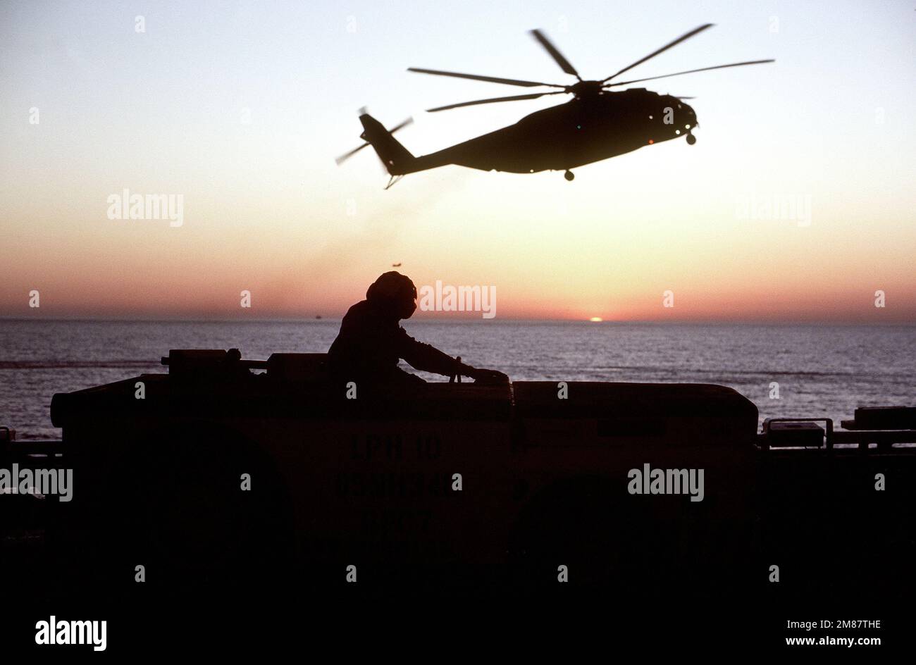 A silhouetted view of a flight deck crewman standing by in a tow ...