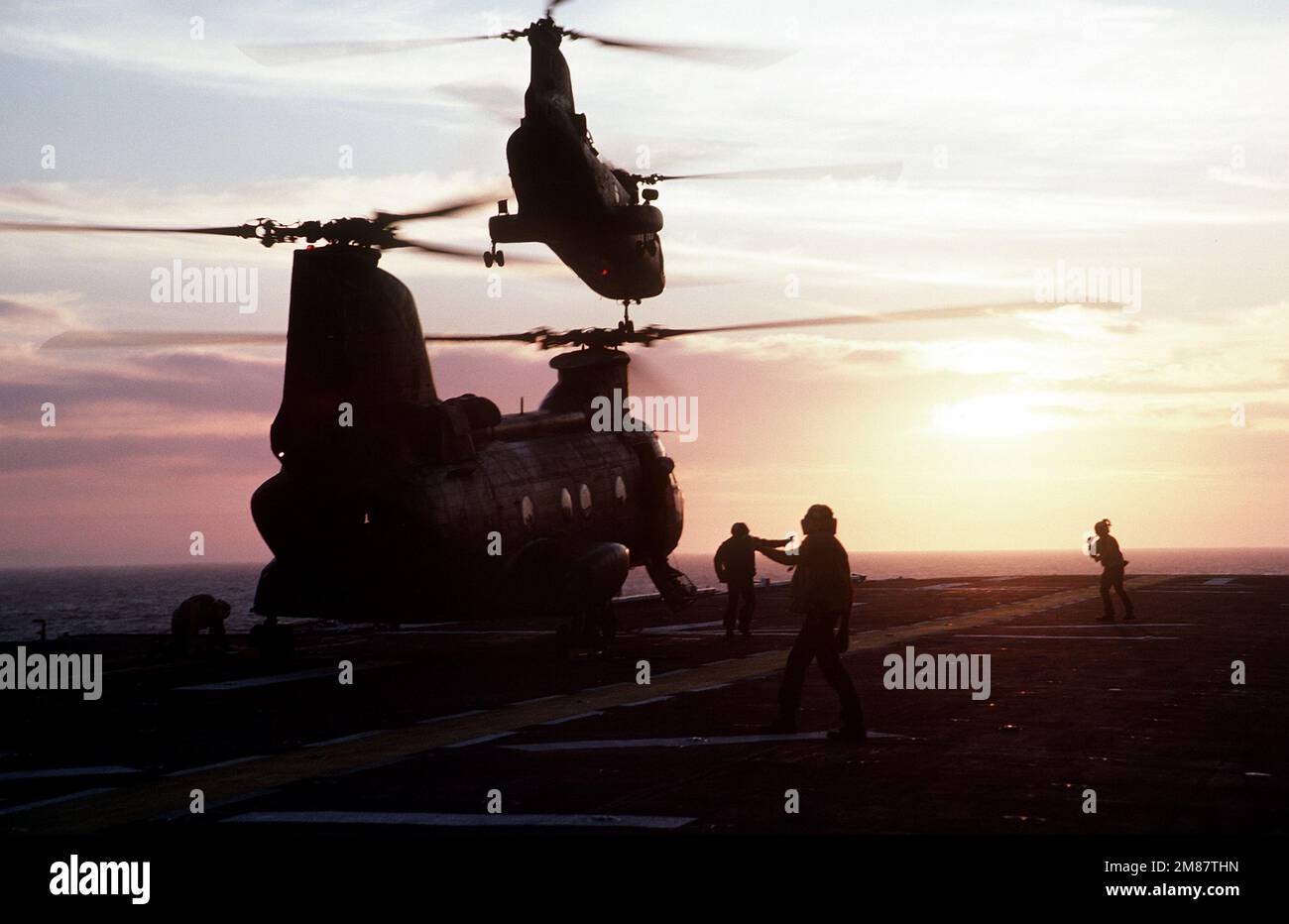 Crew members stand by as a CH-46 Sea Knight helicopter takes off from ...