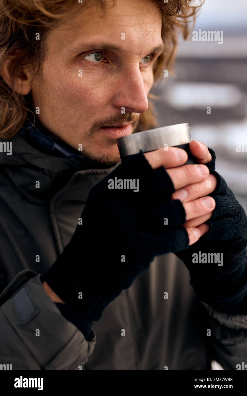 young man walking in snowy forest in winter, drinking tea.Local travel ...