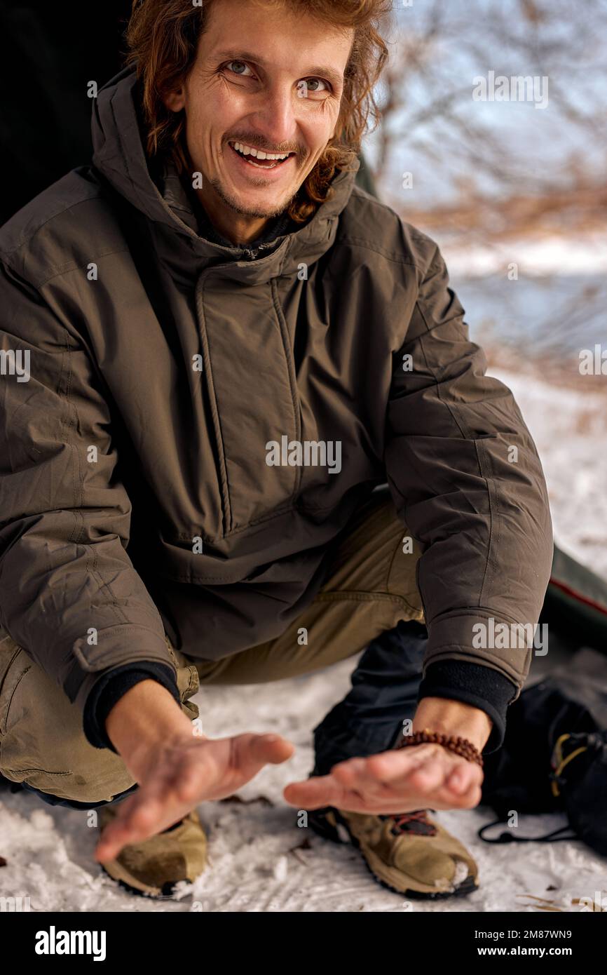 smiling man warm hands by fire, sit next to fire. Travel concept. happy ...