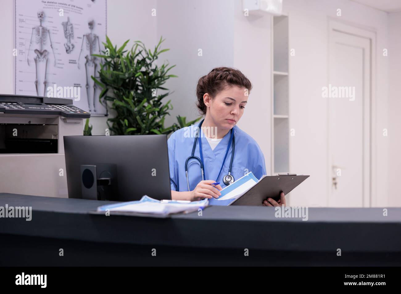 Caucasian nurse working at reception counter looking at medical ...