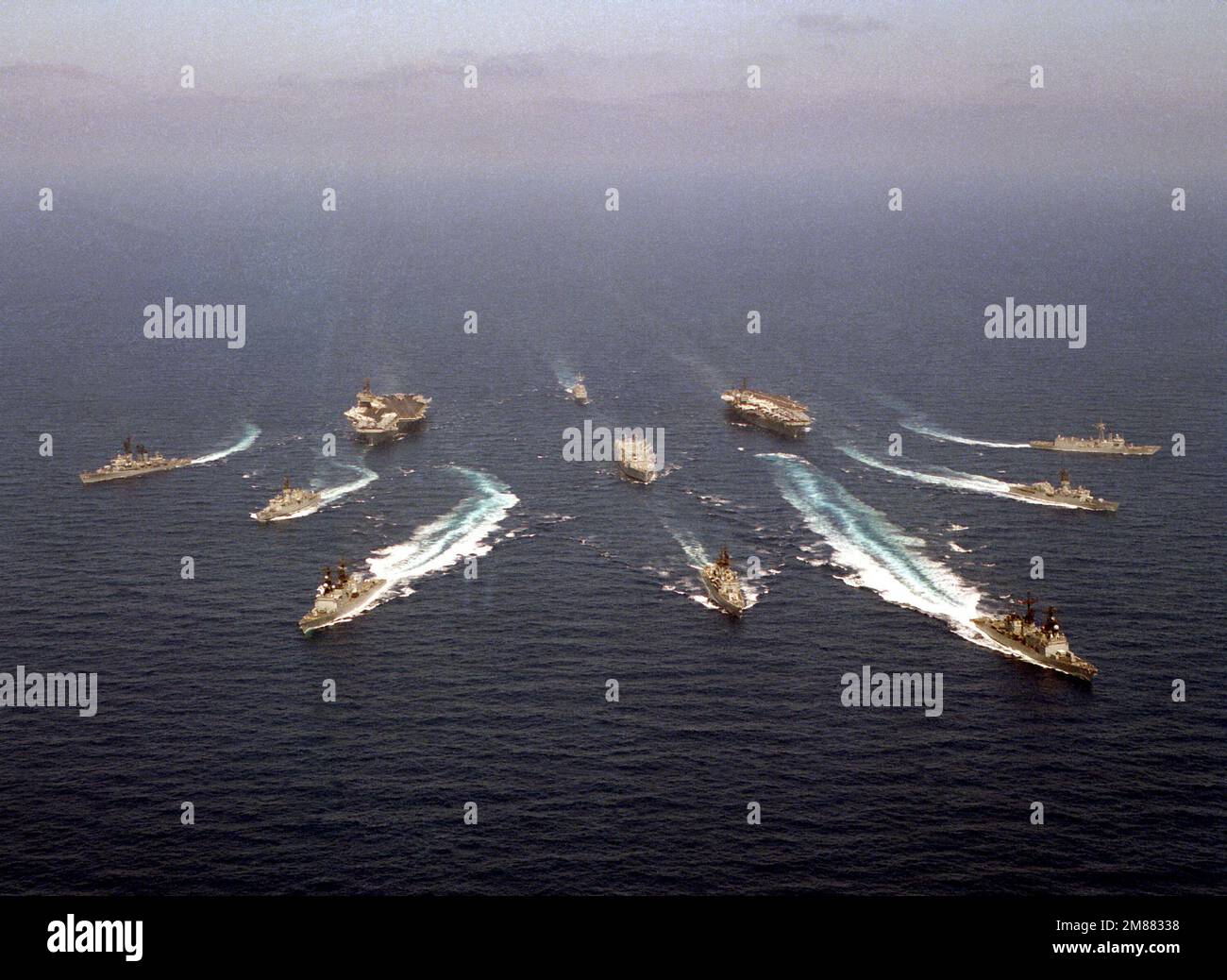 An aerial view of various ships underway in formation. They are ...